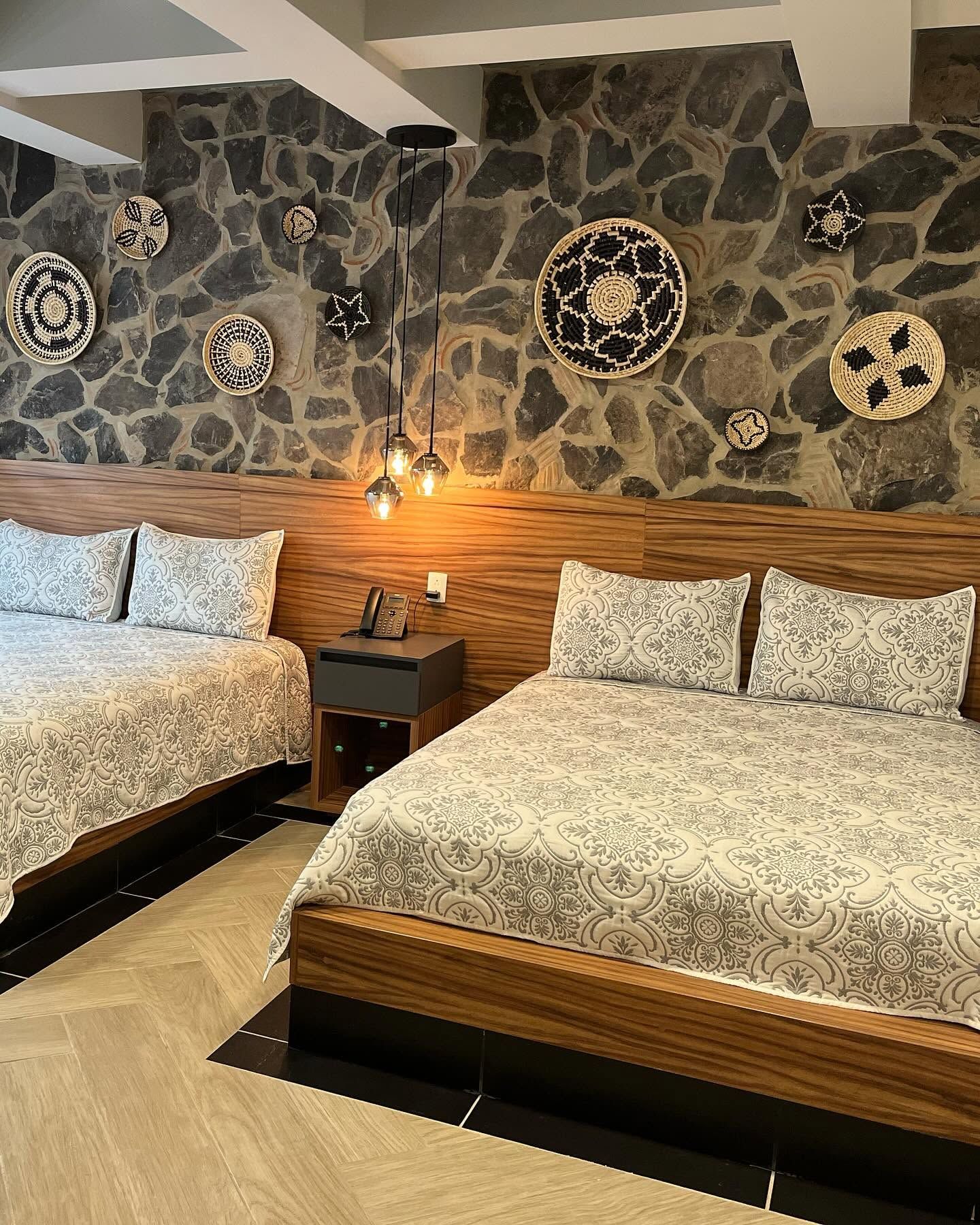 Quarto com duas camas, parede de pedra e pratos decorativos de tecido.