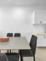 Uma área de refeições moderna com uma mesa retangular, quatro cadeiras e um armário branco com duas portas.