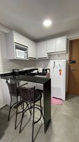 Uma cozinha compacta com armários brancos, micro-ondas, geladeira e duas cadeiras de vime.