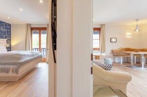 Quarto de hotel moderno com cama, sofá, mesa de jantar e vista para o exterior.