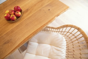 Uma mesa de madeira com uma tigela de maçãs e uma cadeira de vime com almofada.