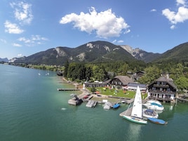 Um hotel na beira do lago com barcos atracados, rodeado por montanhas e vegetação.