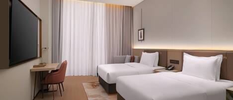 Quarto de hotel com duas camas, uma escrivaninha, uma cadeira e uma televisão.