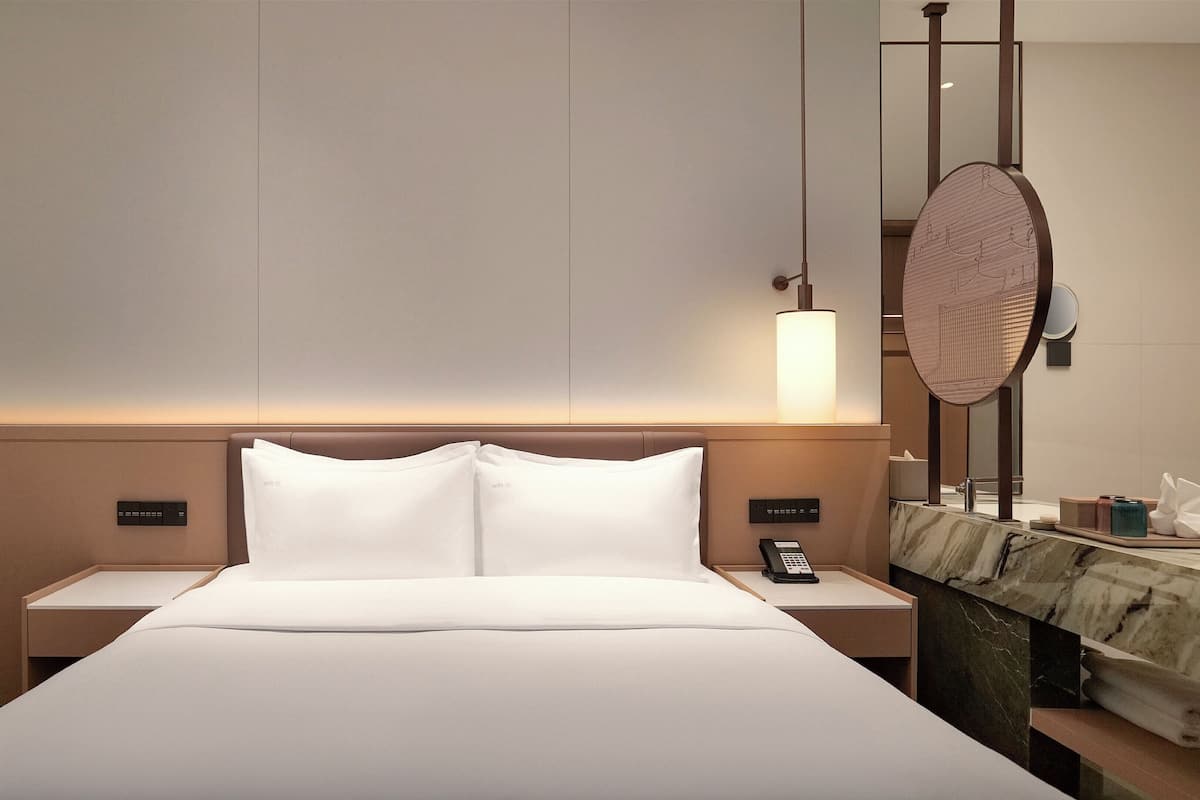 Quarto de hotel com cama, mesas de cabeceira, abajur, espelho e um quadro na parede.