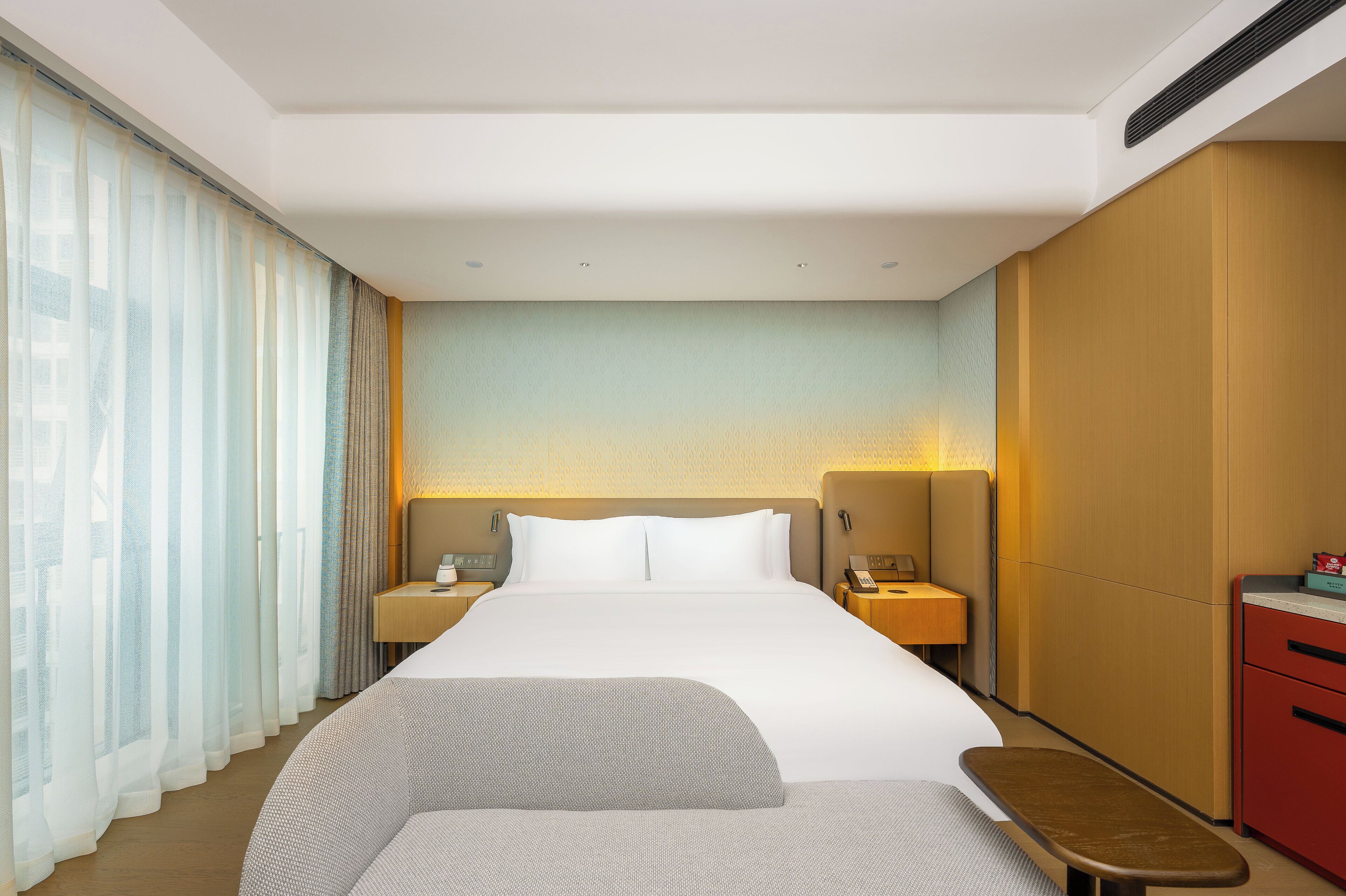 Quarto de hotel moderno com uma cama grande, mesas de cabeceira, escrivaninha e armário.