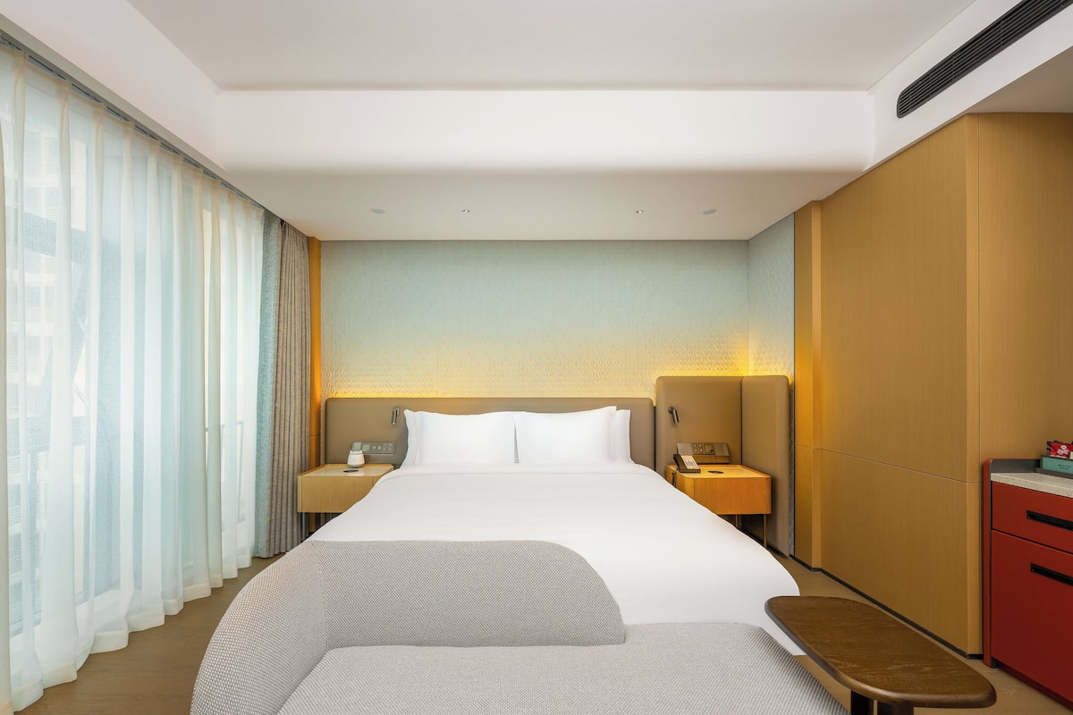 Quarto de hotel moderno com uma cama grande, mesas de cabeceira, escrivaninha e armário.