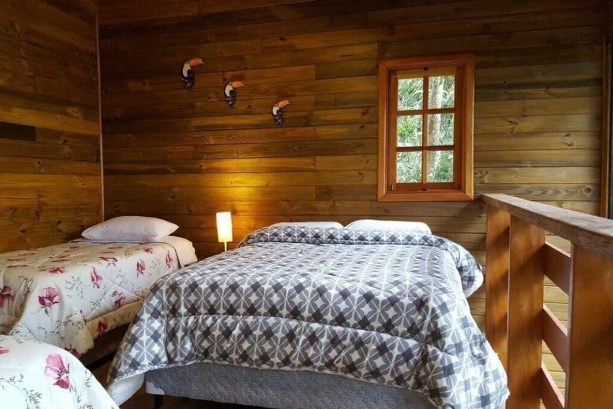 Quarto estilo cabana com duas camas, paredes de madeira, uma janela e luminárias fixadas na parede.