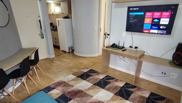 Um espaço de estar compacto com uma cama, uma escrivaninha e uma TV fixada na parede.
