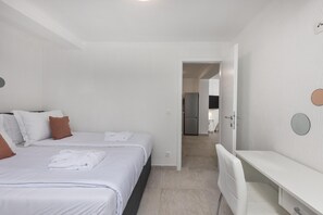 Quarto de hotel com duas camas, uma escrivaninha e um banheiro visível através de uma porta aberta.