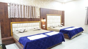 Quarto de hotel com duas camas, cada uma com cabeceira e colcha azul. Há cortinas nas janelas e painéis de madeira nas paredes.
