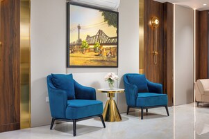 Um hall moderno com dois poltronas azuis, uma mesa redonda dourada e um quadro de uma ponte.