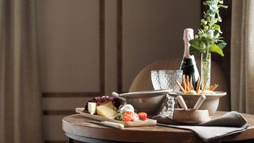 Uma mesa com diversos alimentos, incluindo queijo, tomates e biscoitos, além de uma garrafa de champanhe e um vaso com flores.
