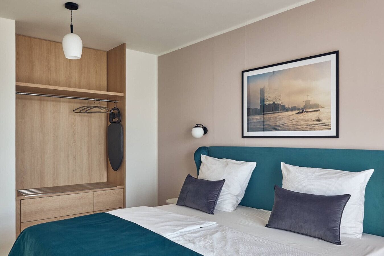 Quarto de hotel com cama, guarda-roupa, candeeiro pendente e quadro na parede.
