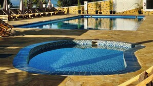 Piscina com borda azulejada, espreguiçadeiras e guarda-sóis.