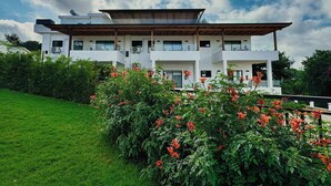 Uma casa moderna de vários andares com telhado plano, grandes janelas e um jardim bem cuidado com plantas floridas.