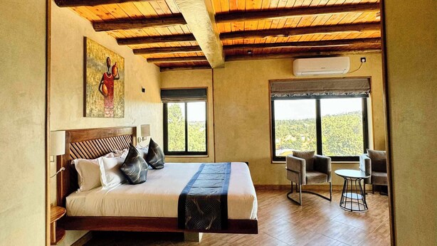 Um quarto amplo com uma cama grande, uma mesa pequena e uma janela com vista.