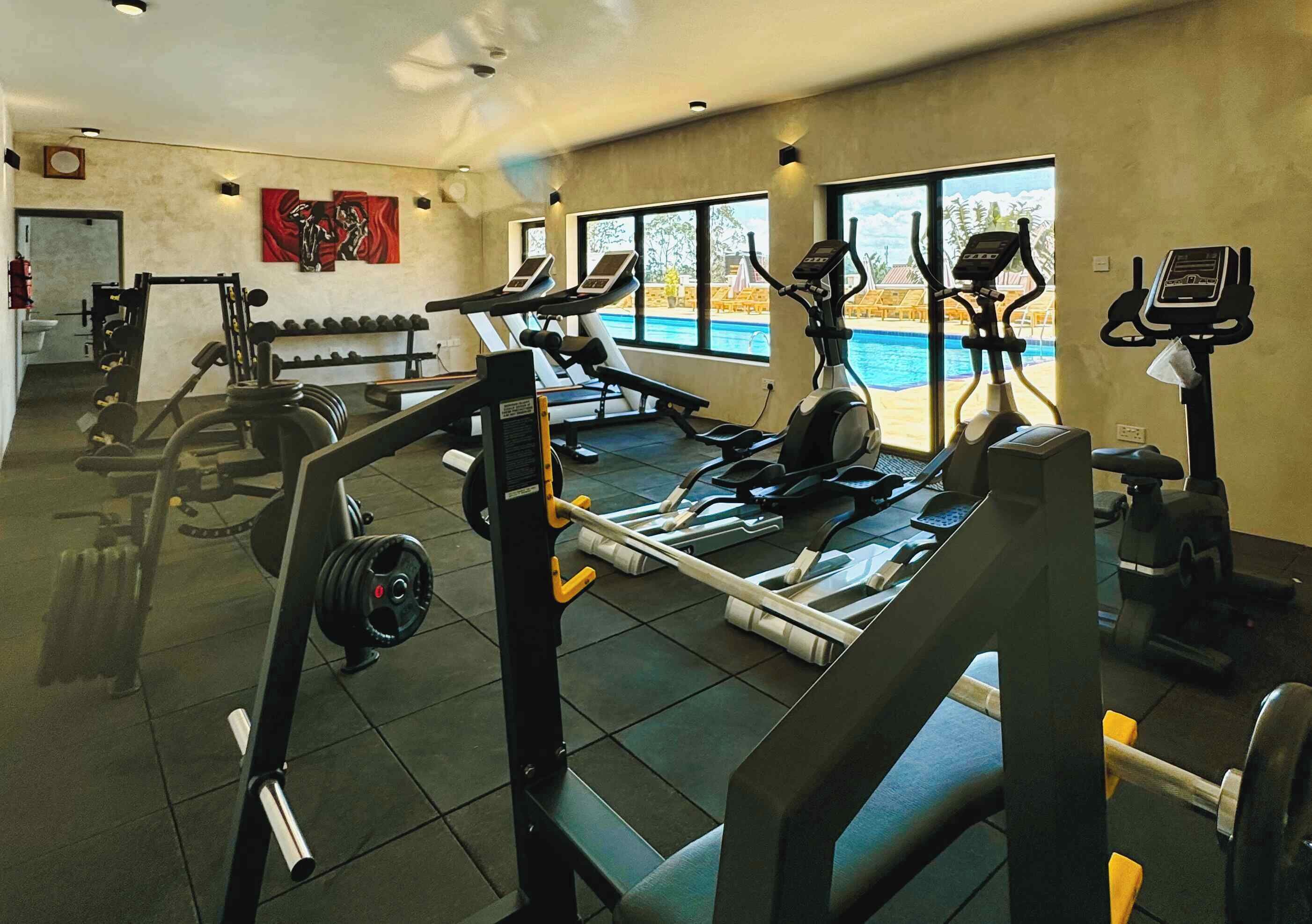 Academia com equipamentos de cardio, aparelhos de musculação e vista para uma piscina.