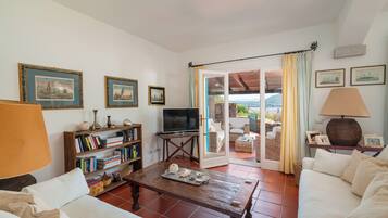 Sala de estar com televisão, estantes de livros, mesa de centro e vista para um pátio externo através de uma porta de vidro.