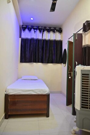 Quarto com uma cama de solteiro, janela com cortinas, porta e radiador.