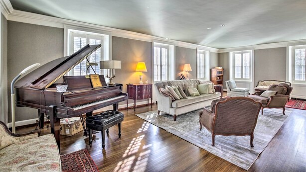Uma sala de estar ampla, com um piano de cauda, um conjunto de sofás e um tapete estampado.
