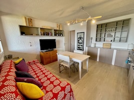 Um espaço de estar compacto com sofá, televisão, mesa de jantar e kitchenette.