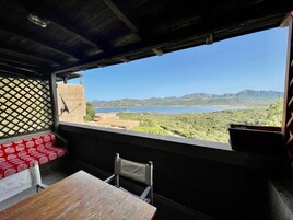Varanda com mesa e cadeiras de madeira, com vista para uma paisagem deslumbrante com um corpo de água e colinas.