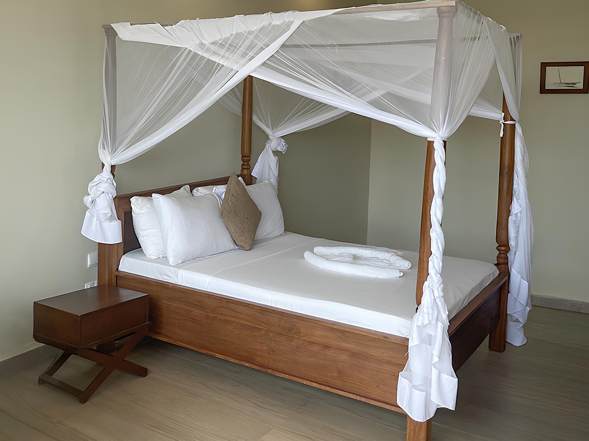 Uma cama de dossel com cortinas, roupa de cama branca, cabeceira de madeira e mesa de cabeceira.