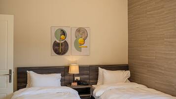 Quarto de hotel moderno com duas camas, uma mesinha de cabeceira com abajur e uma obra de arte na parede.