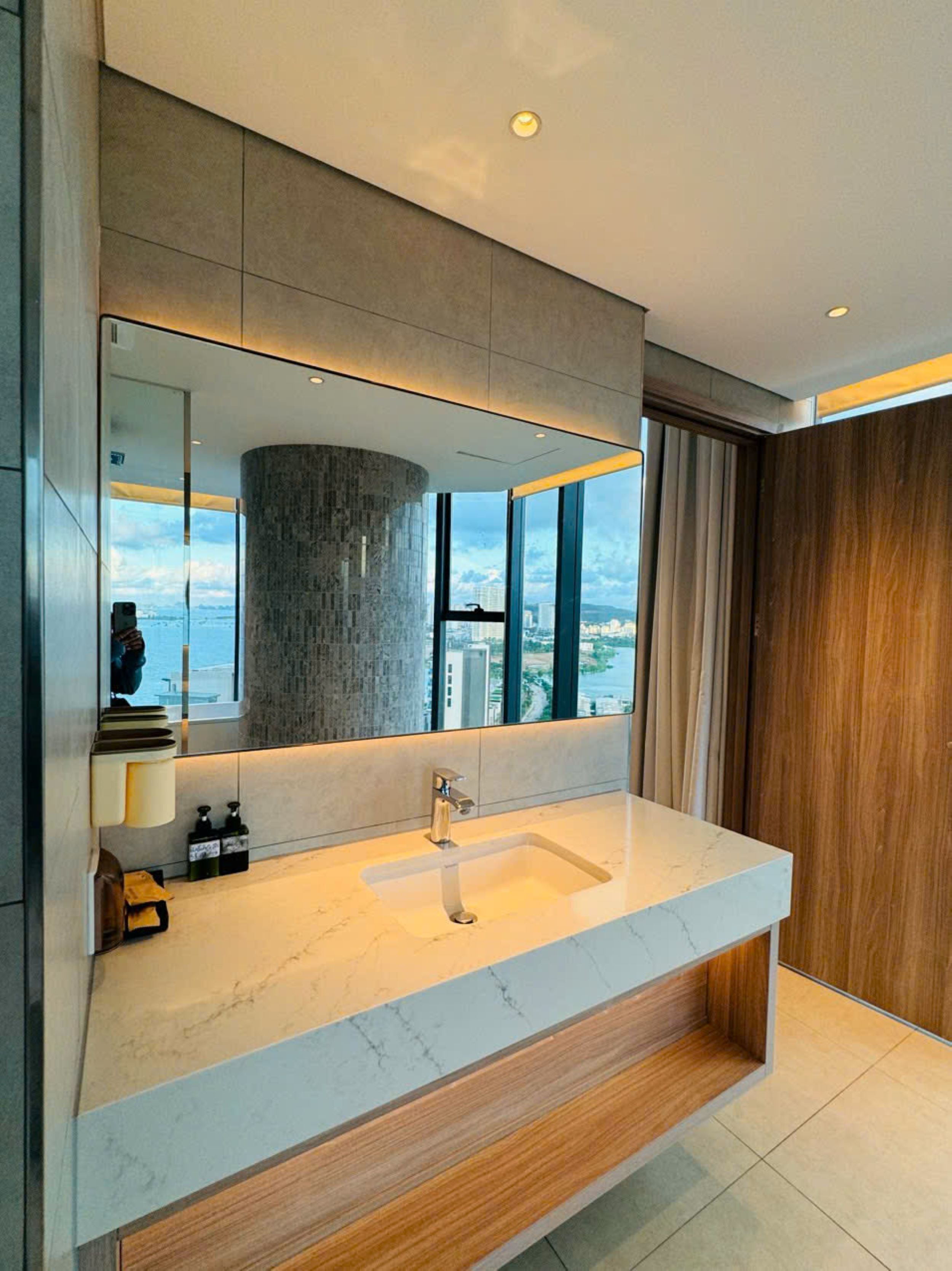 Uma casa de banho moderna com um espelho grande, uma pia de mármore e vista para a cidade.