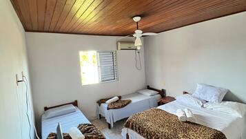 Quarto de hotel com duas camas de solteiro, uma cama de casal, uma televisão e um ventilador de teto.