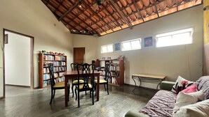 Um quarto espaçoso com teto alto, área de jantar com mobiliário de madeira, sofá verde e estante repleta de livros.