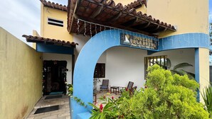 Pátio com um arco azul, área de estar com cadeiras e mesa, e diversos vasos com plantas.