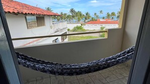 Uma varanda com uma rede, piso de azulejos e vista para edifícios e palmeiras.