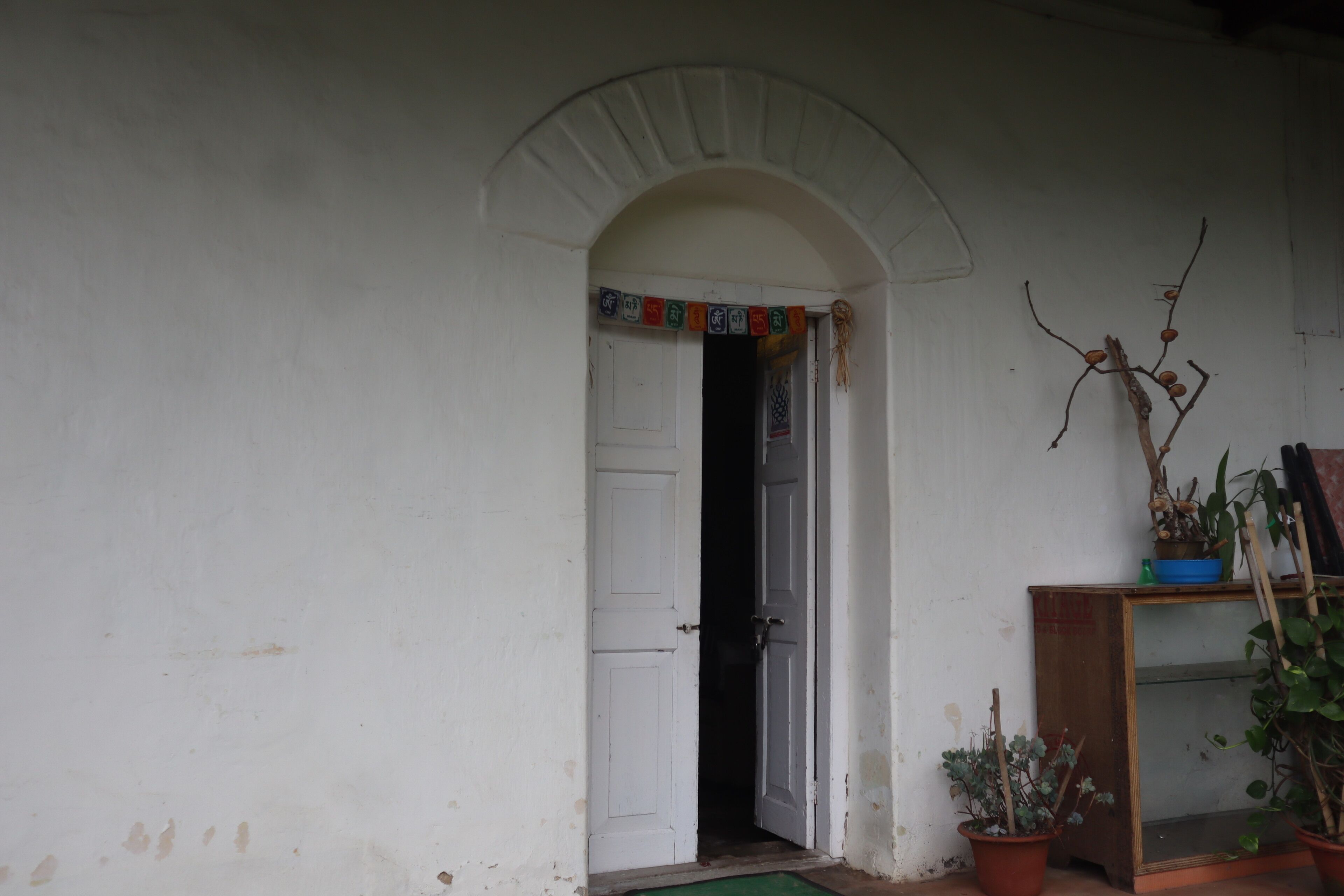 Uma entrada com um arco simples, uma porta e um pequeno nicho com plantas em vasos ao lado.