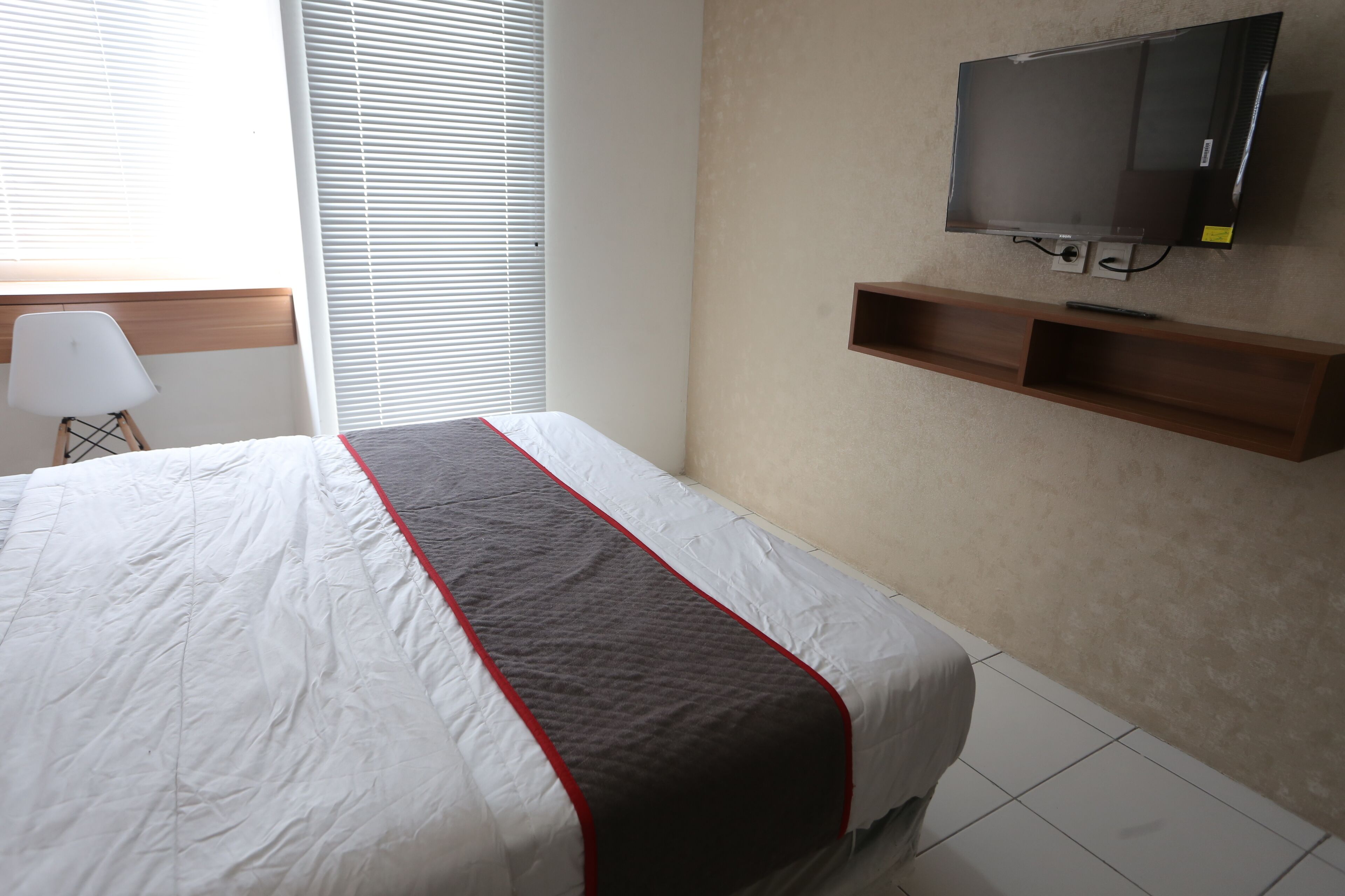 Quarto de hotel com uma cama, televisão na parede e janela com persianas.