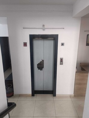 Um elevador com painel de controle, uma porta com um rasgo visível e um corrimão.