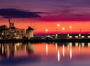 Cena à beira-mar com um moinho, edifícios e uma superfície aquática calma que reflete luzes.