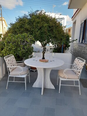 Uma mesa redonda ao ar livre com duas cadeiras, rodeada por uma pequena árvore e um vaso com planta.