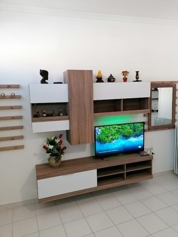 Uma sala de estar moderna com uma TV de tela plana, prateleiras de madeira e objetos decorativos.