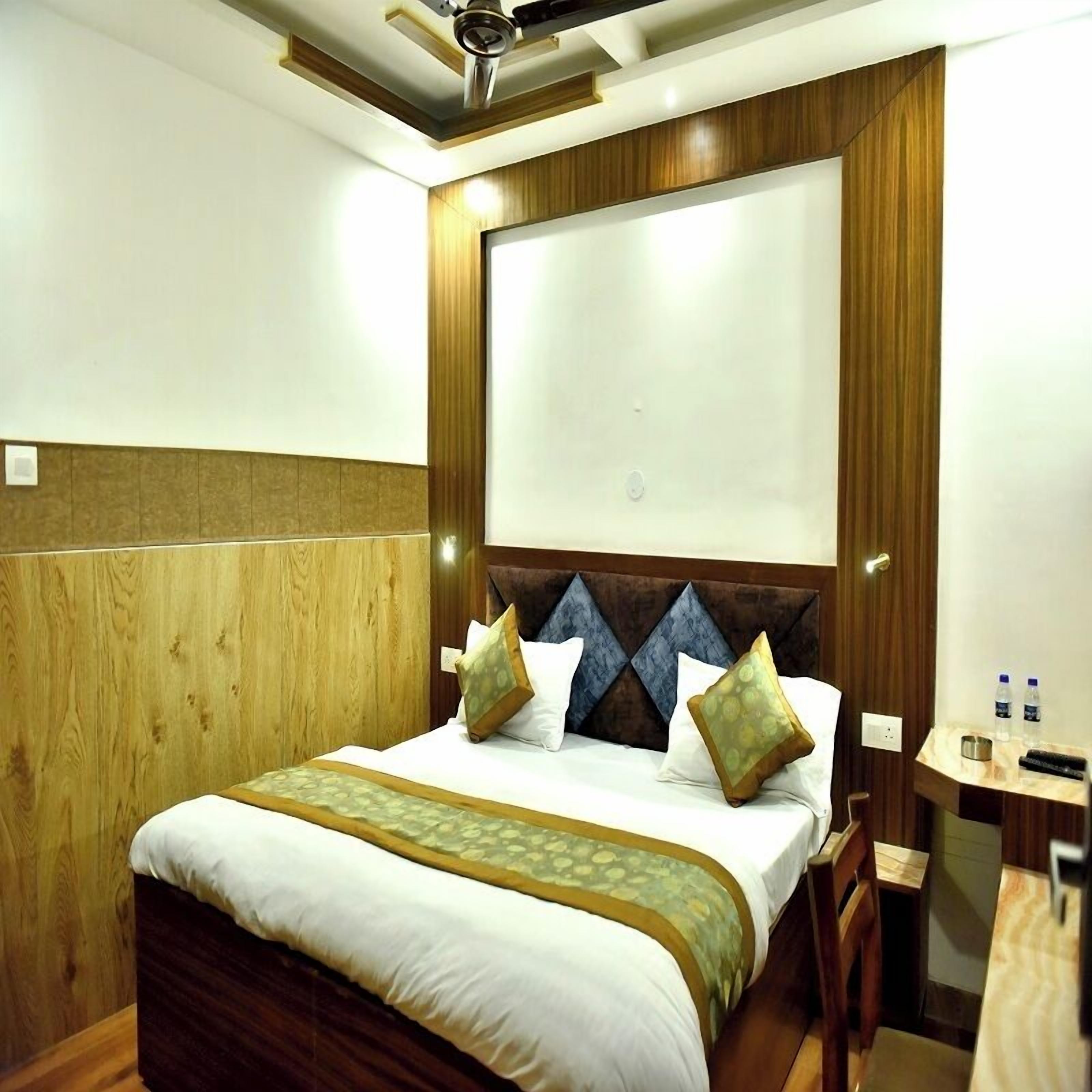 Quarto de hotel com uma cama grande, painéis de madeira nas paredes, um ventilador de teto e uma pequena mesa com uma cadeira.