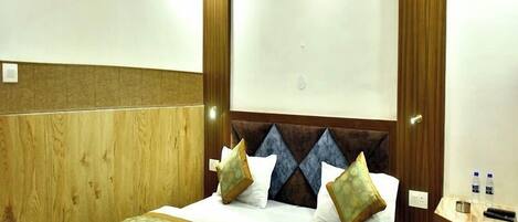 Quarto de hotel com uma cama grande, painéis de madeira nas paredes, um ventilador de teto e uma pequena mesa com uma cadeira.