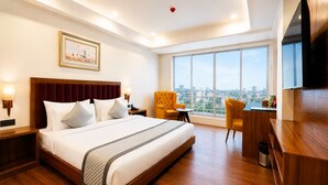 Quarto de hotel com uma cama grande, uma escrivaninha, duas cadeiras, televisão e vista para a cidade.
