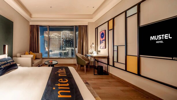 Quarto de hotel moderno com uma cama grande, uma escrivaninha e vista para a cidade.