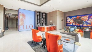 Um hall de hotel moderno com  área de bar, assentos e uma tela grande exibindo 'HELLO' e 'MUSTEL'.