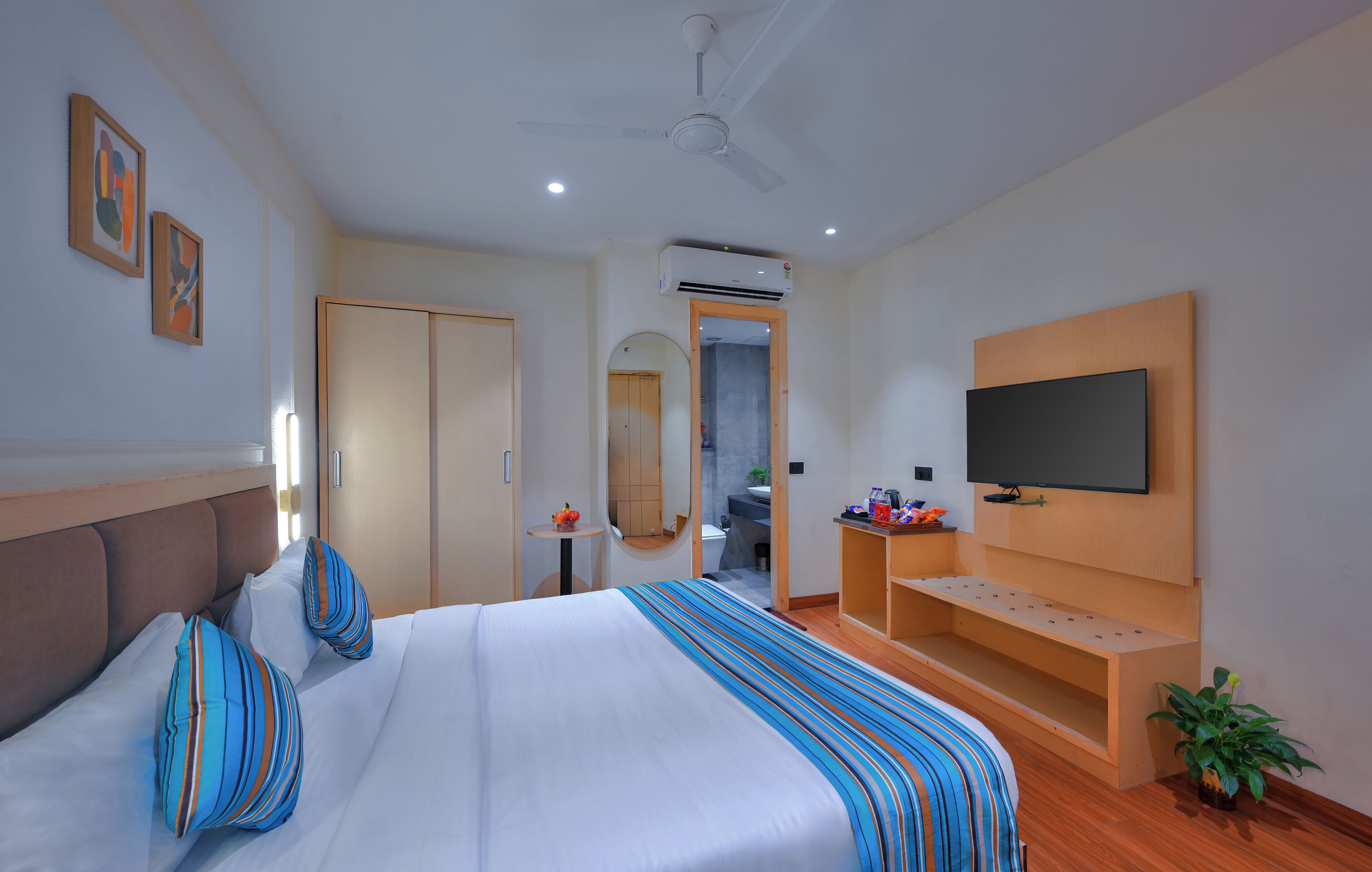 Quarto com cama, televisão, ventoinha no teto e banheiro visível por um arco.