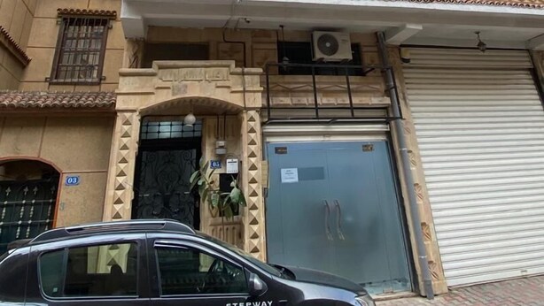 Um edifício com vários andares, varandas, uma porta de garagem e uma placa indicando um estabelecimento comercial.