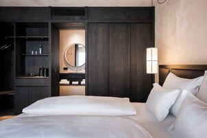 Quarto de hotel moderno com uma cama grande, um guarda-roupa embutido, uma toucador com espelho e um abajur.