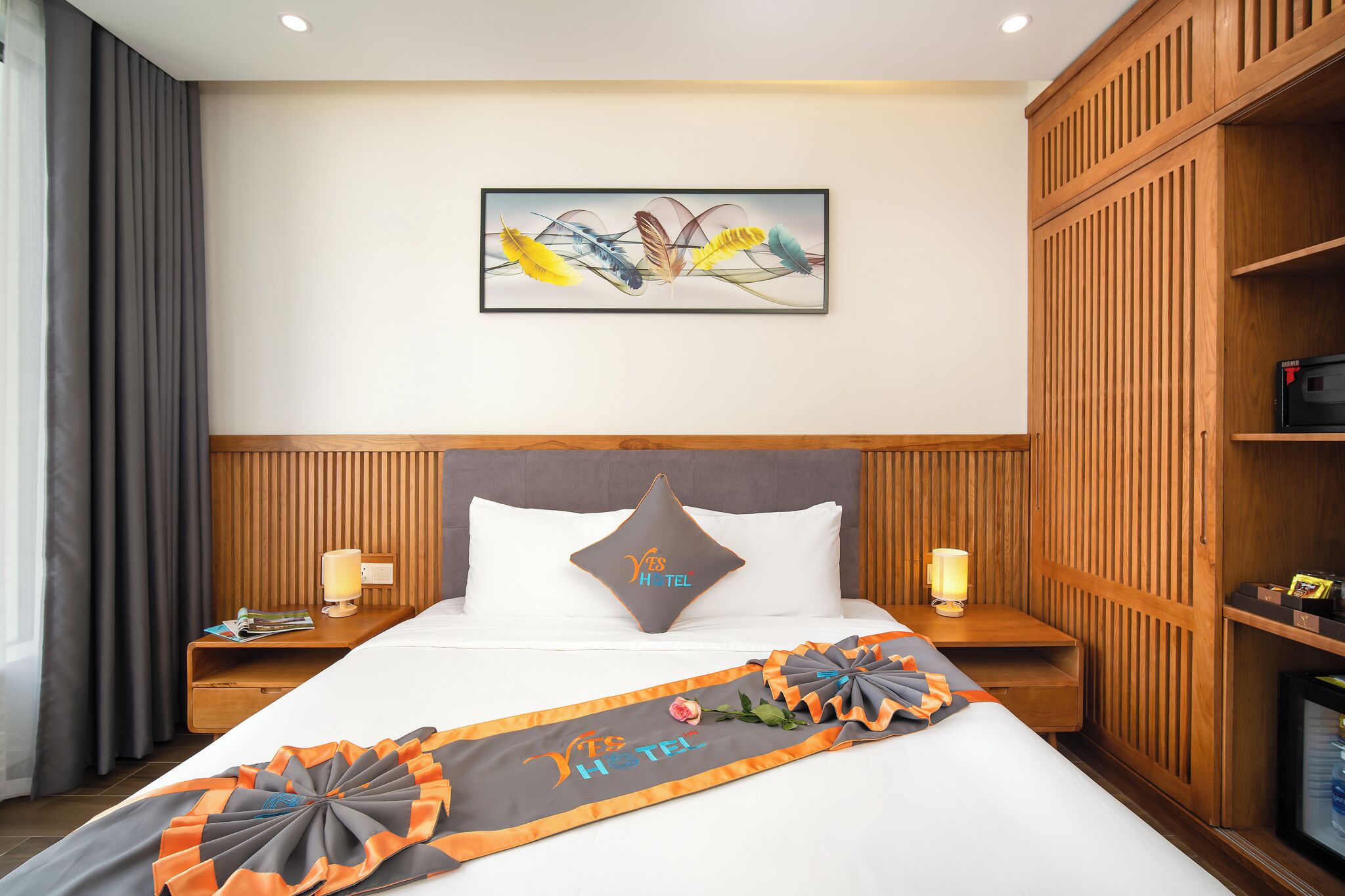 Quarto de hotel com cama, mesa de cabeceira, luminária, guarda-roupa de madeira e uma obra de arte na parede.