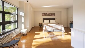 Quarto moderno com uma grande janela, uma cama, uma cadeira e uma mesinha.