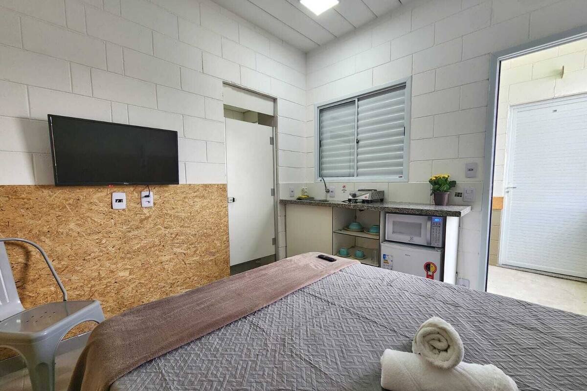 Quarto de hotel com cama, televisão, cozinha compacta e porta de correr.